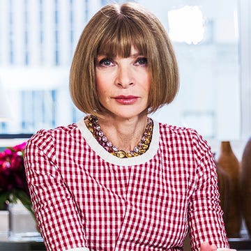 a woman in a red and white checkered dress stares at the camera, she has a bob haircut with bangs and wears a chunky necklace