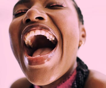 close up shot of a young black woman expressively laughing into camera in front of a pink background stock photo