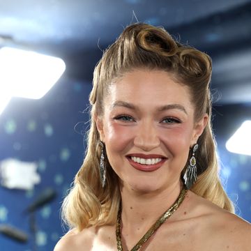 a woman smiles at the camera, she wears a gold halter top gown and dangling earrings