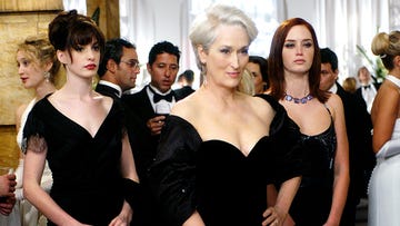 the devil wears prada film still featuring anne hathaway, meryl streep, and emily blunt in character all wearing formal black dresses at a cocktail party